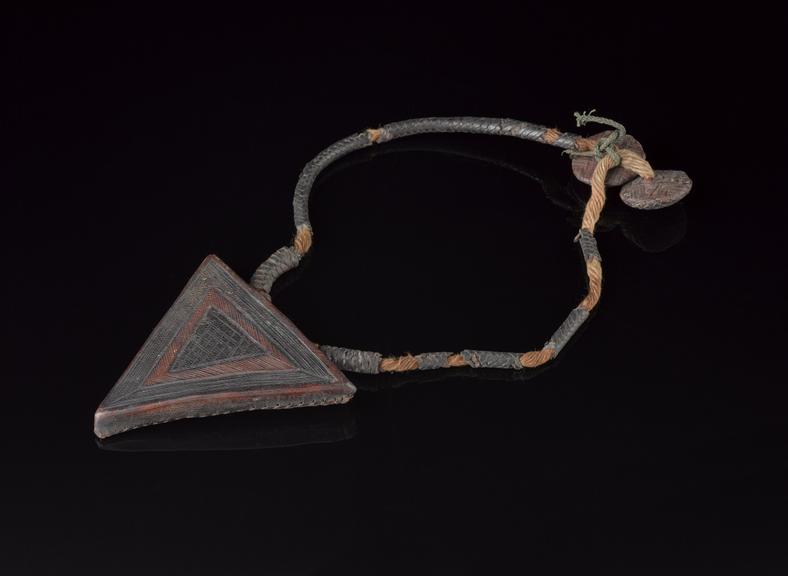 Triangular leather amulet suspended from cord of fibre and plaited ...