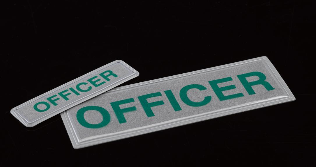Pair of grey reflective badges marked 'OFFICER' in green lettering ...